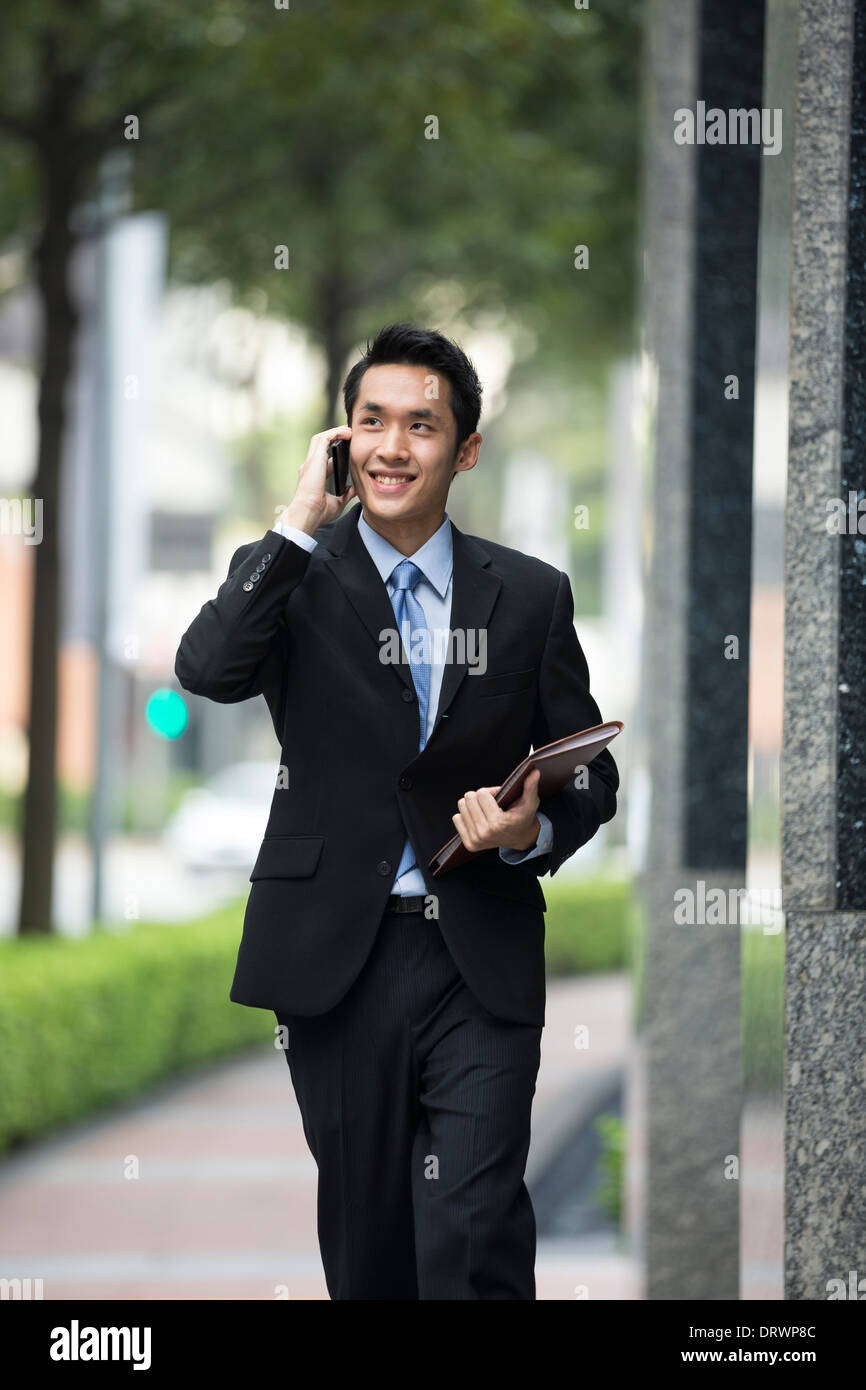 Chinese business Man using his cell phone outdoors in modern Asian city ...