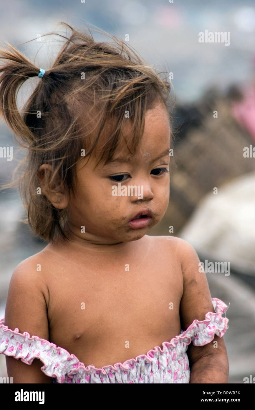 A young girl living in poverty is standing amidst trash at the toxic ...