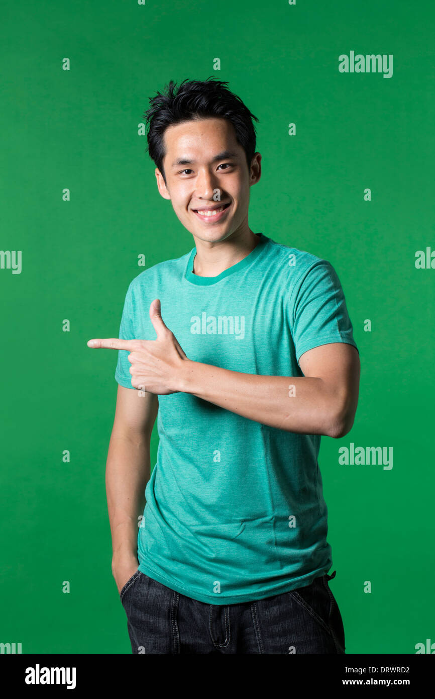 Portrait of a happy Asian man pointing at something. Green background ...