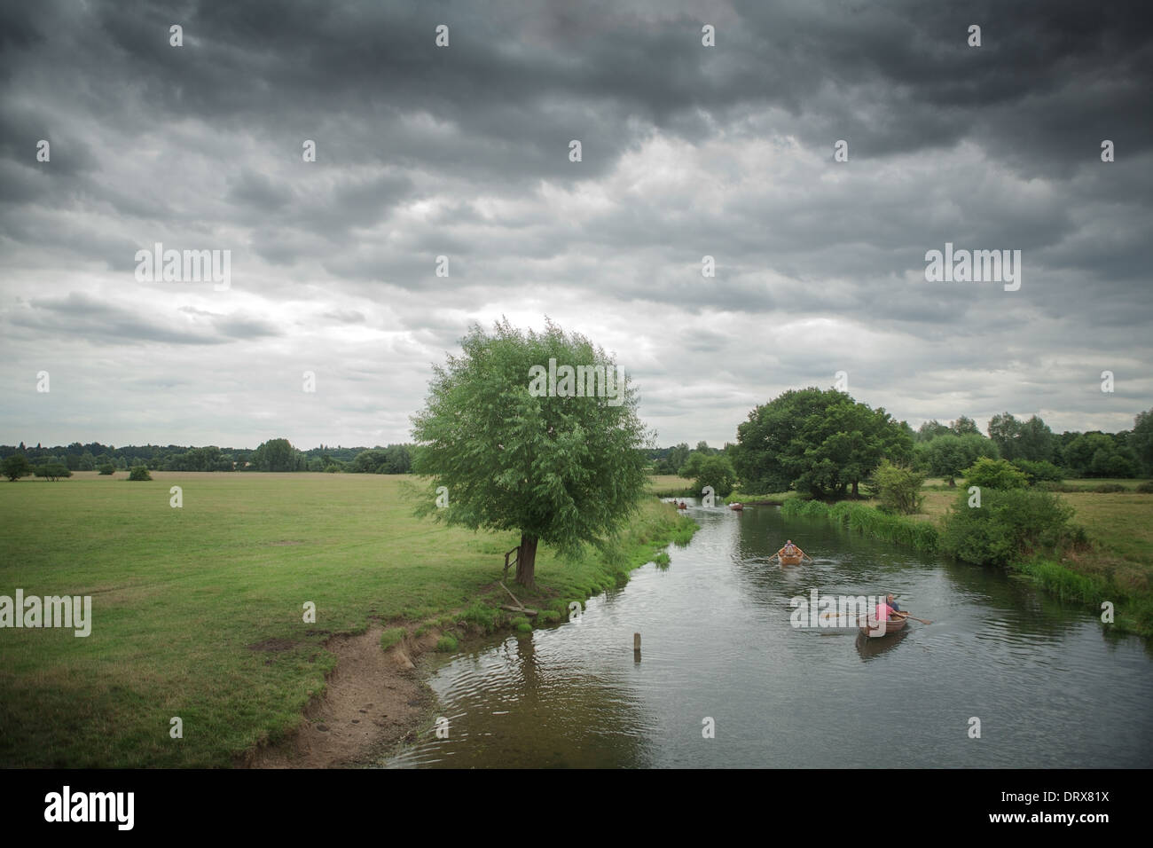 Overcast sky looming over a stream with 2 rowing boats rowing down the ...