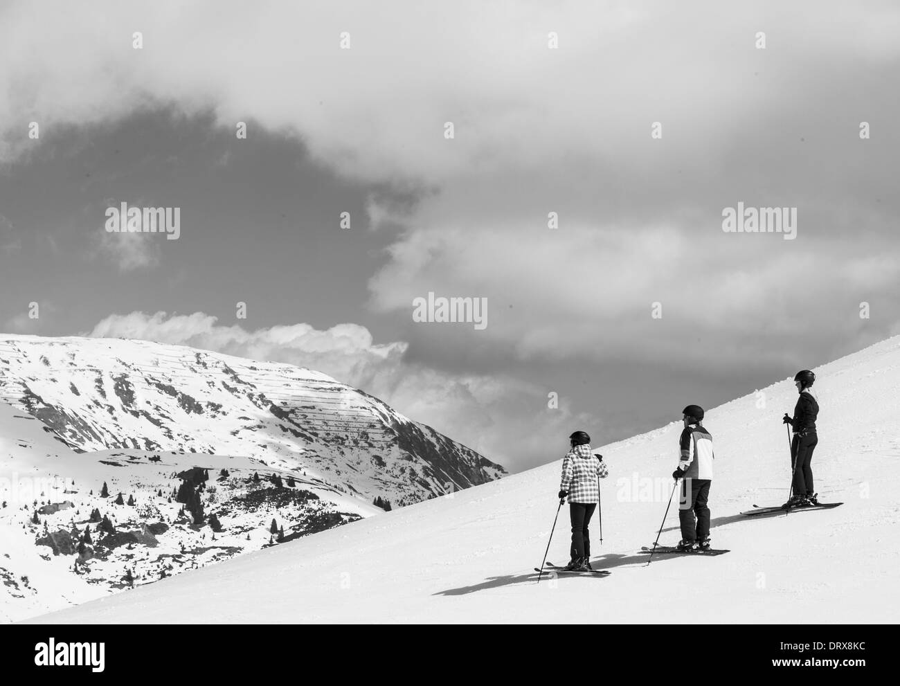 Three skiers wait at the top of a mountain in a row, ready to ski down ...