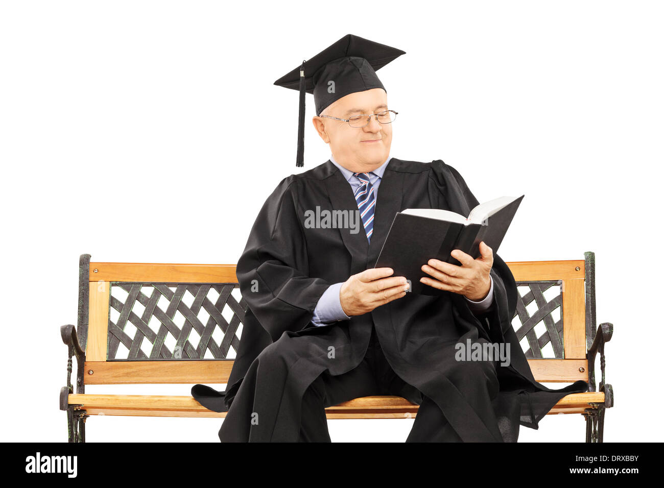 Mature man in graduation gown seated on bench reading a book Stock ...