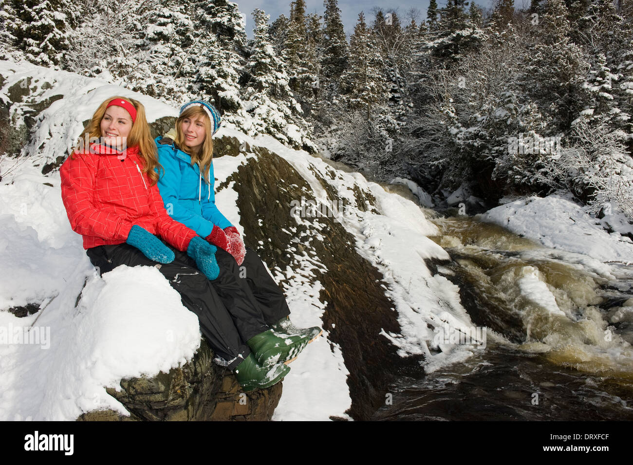 Two girls sit on snow covered rocks on a lakeshore in winter Stock ...