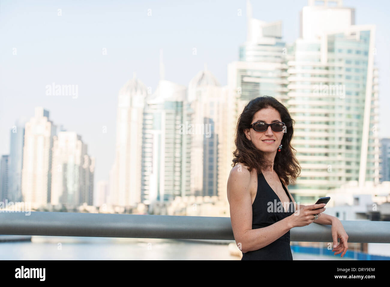 Woman leaning against railing with smarphone in hand, skyscrapers in ...