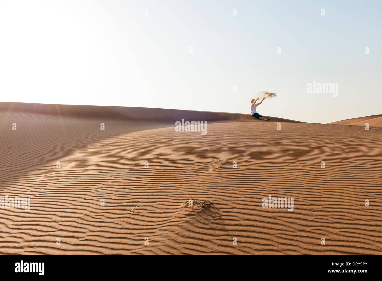 Teenage boy sitting on desert dune, throwing sand in air Stock Photo ...