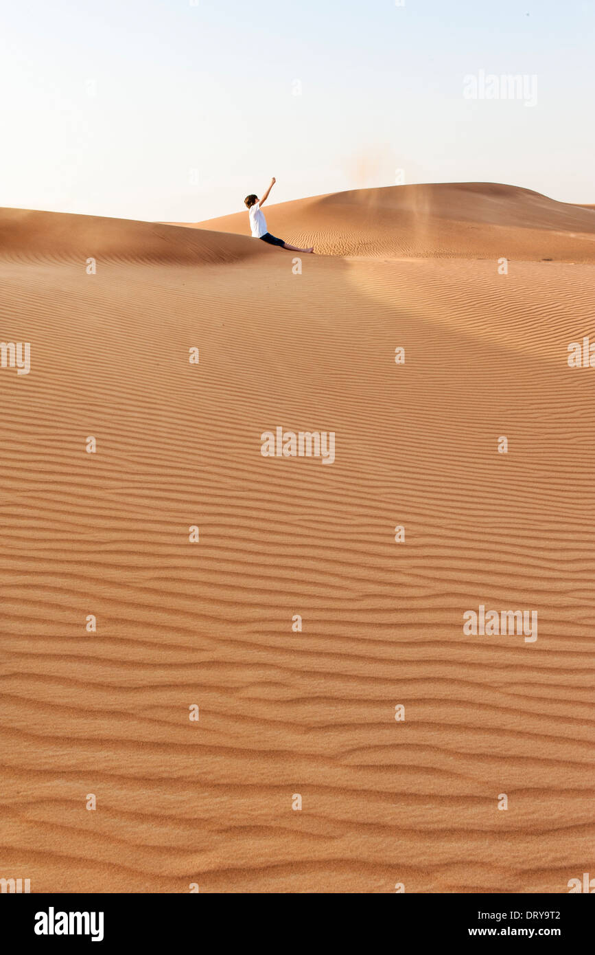 Teenage boy sitting on desert dune, throwing sand in air Stock Photo ...