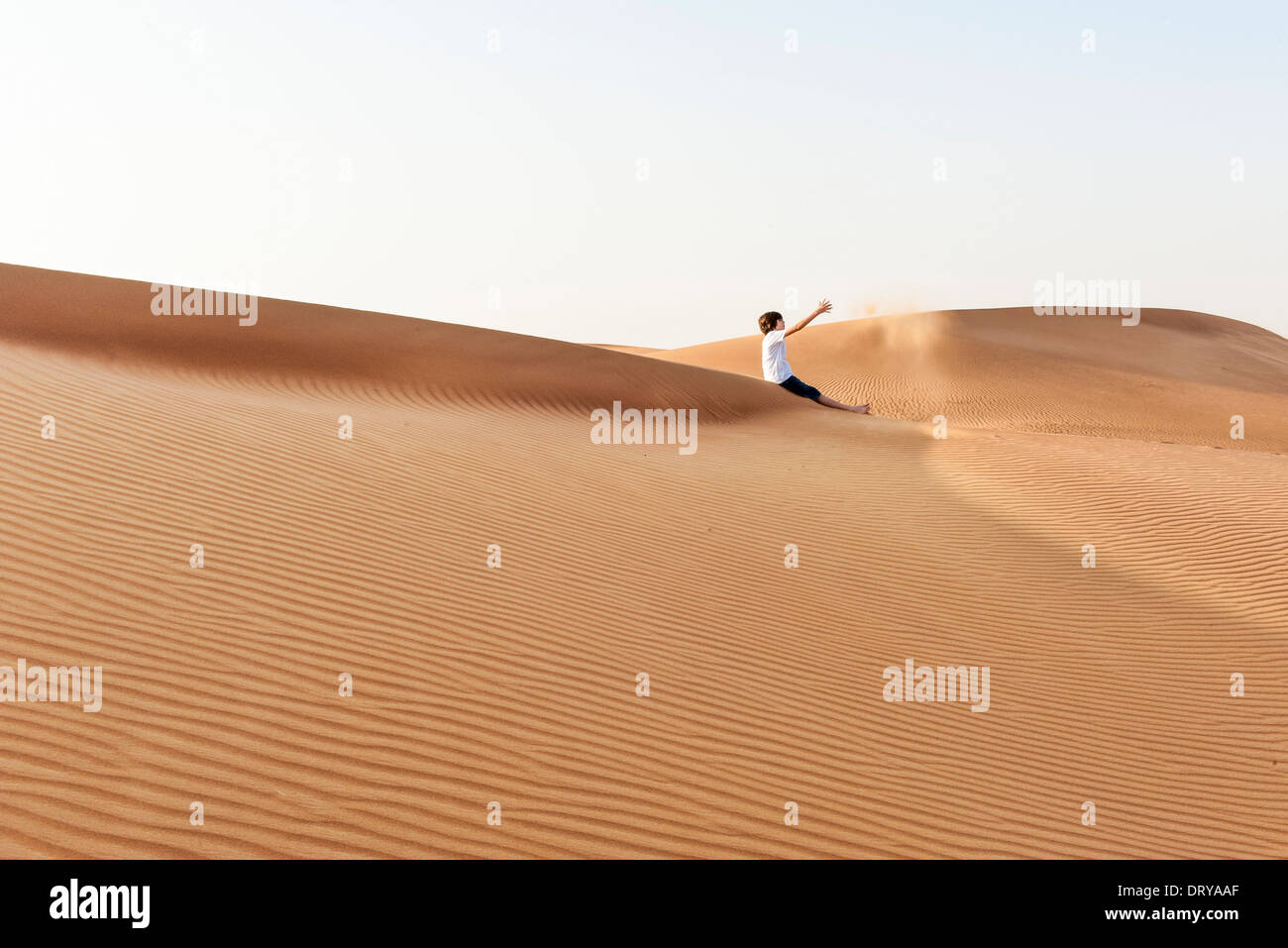 Teenage boy sitting on desert dune, throwing sand in air Stock Photo ...