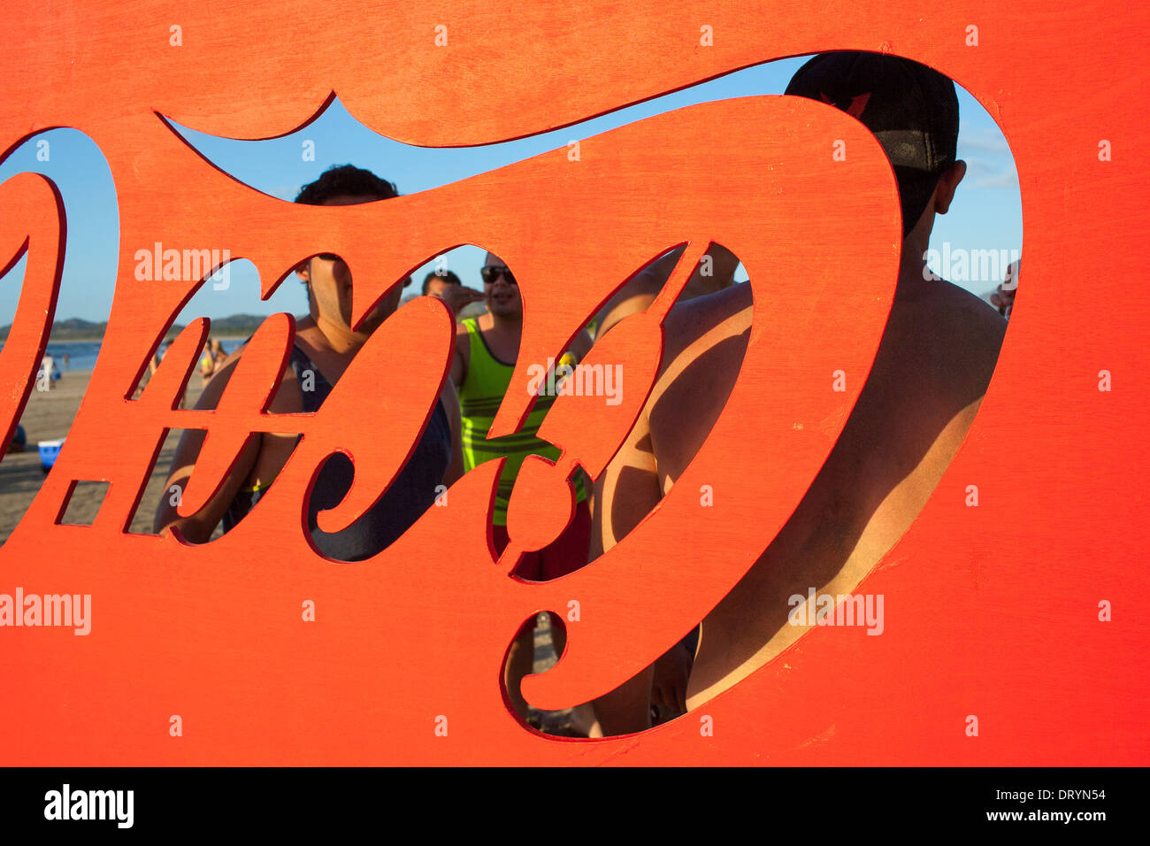 Young people stand and sit next a Coca Cola sign on the beach in Playa ...