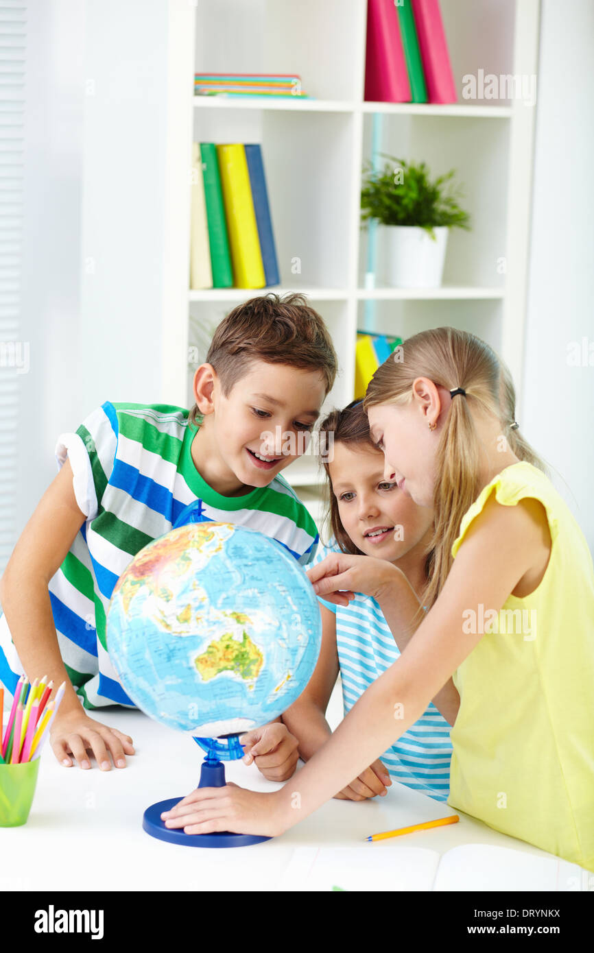 Portrait of curious classmates at workplace studying globe in classroom ...