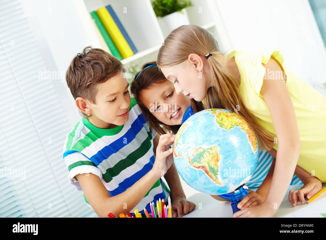 Portrait of happy classmates at workplace studying globe in classroom ...