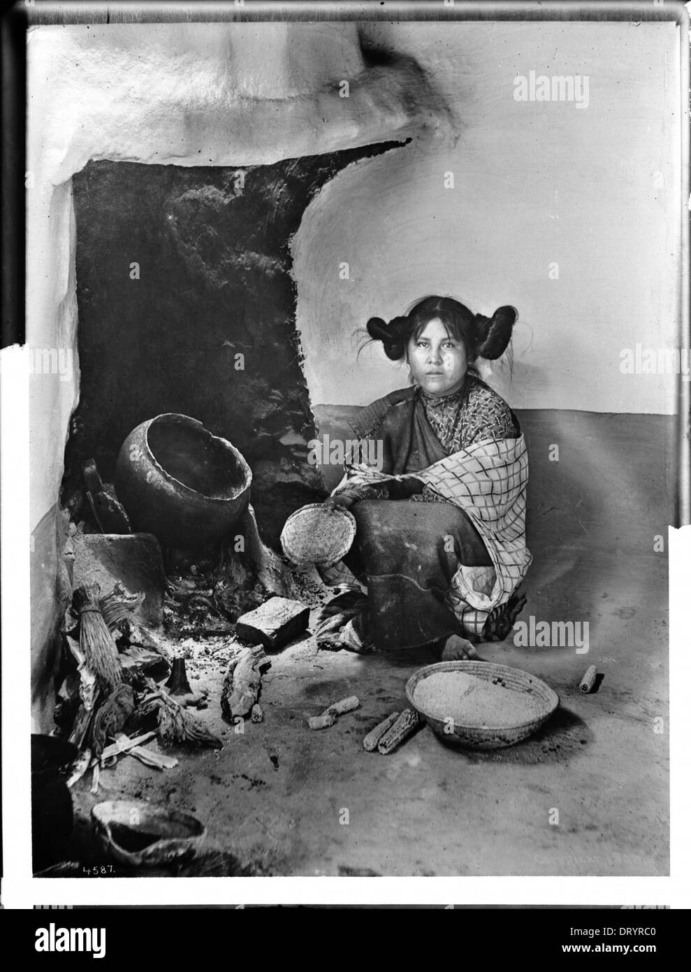 A Hopi maiden is shown drying cornmeal at a fireplace in Mishongnovi or ...