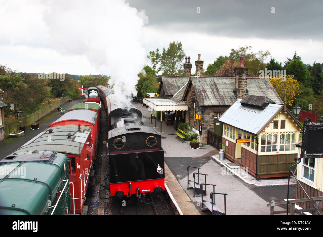 A steam train arrives at a station platform with a signal box in the ...