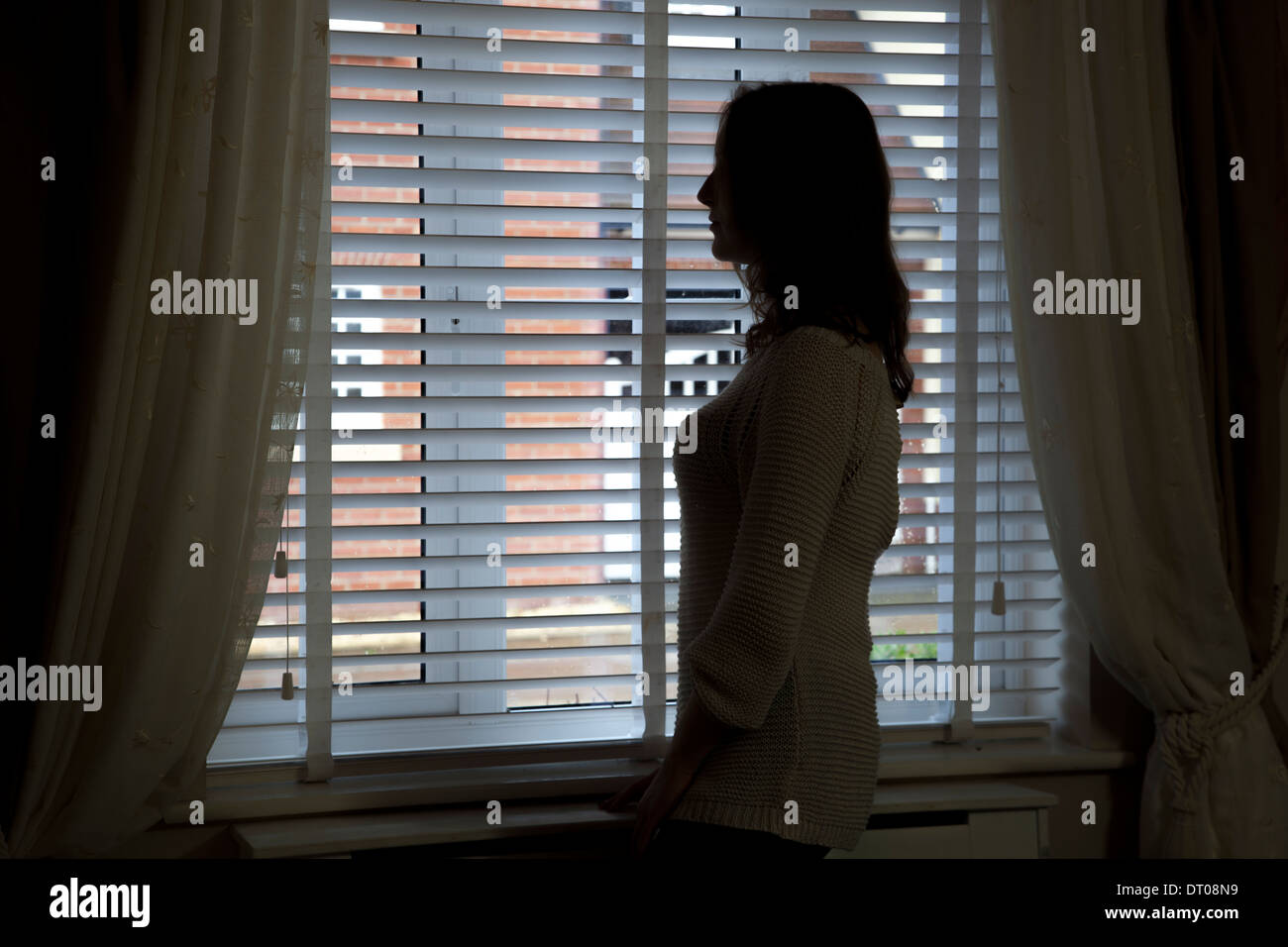 Silhouette of woman standing by a window. Over shoulder back/side view ...