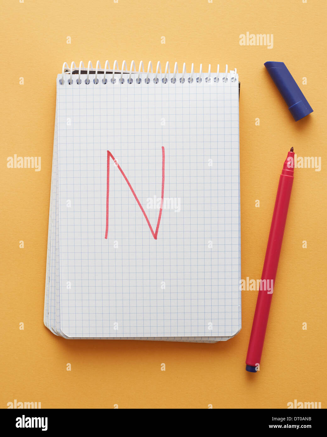 N letter handwritten in notebook page on yellow background alphabet ...