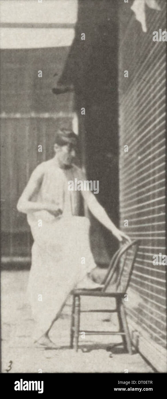 This photograph shows a draped woman stepping on a chair, reaching up ...