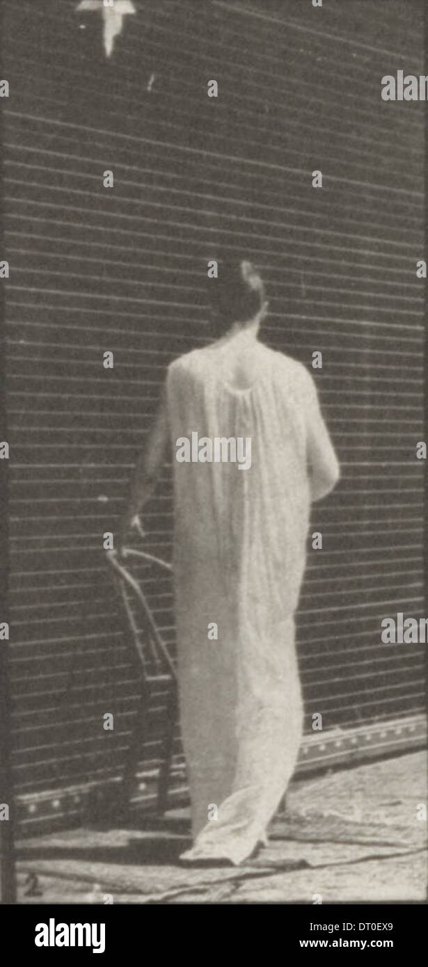A photograph of a draped woman stepping on a chair, reaching up, and ...