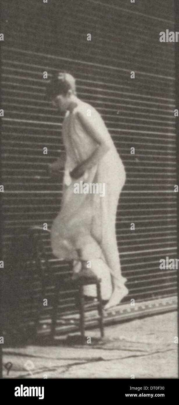 A draped woman is photographed stepping on a chair and reaching up ...