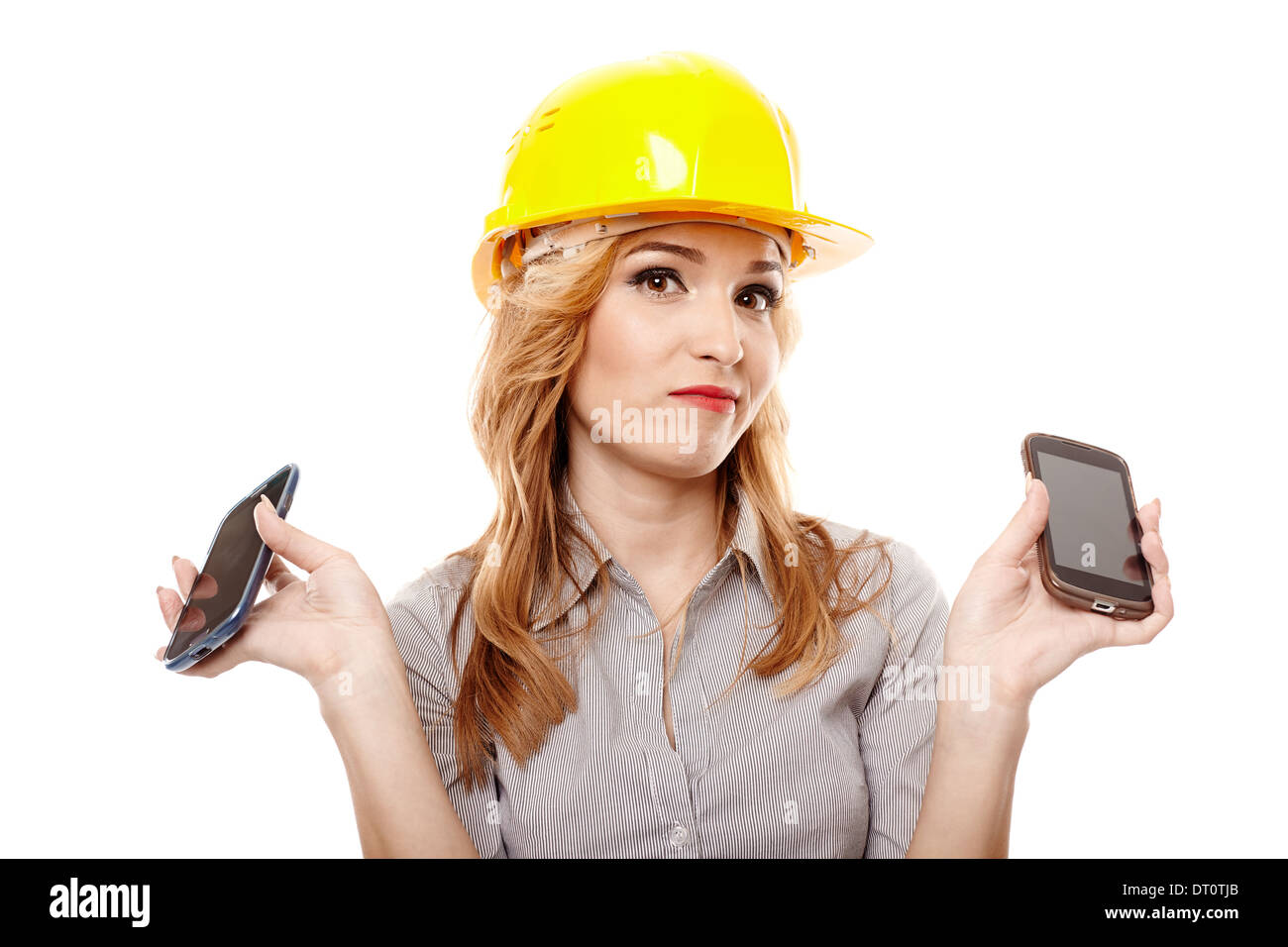 Bored woman engineer with protection helmet holding two cell phones ...