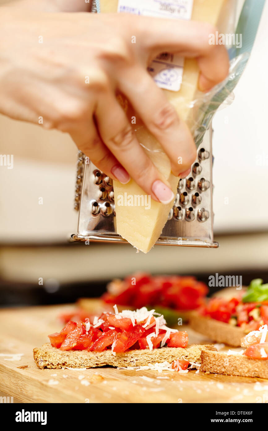 Closeup of cook's hands grating a lump of parmesan over tomato ...