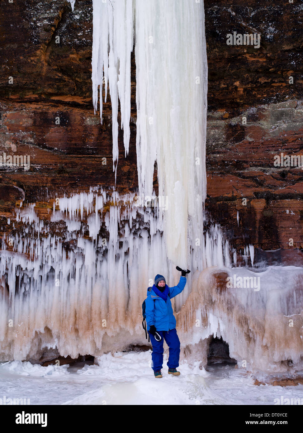 A woman stands under an enormous icicle at the Apostle Island Ice Caves ...