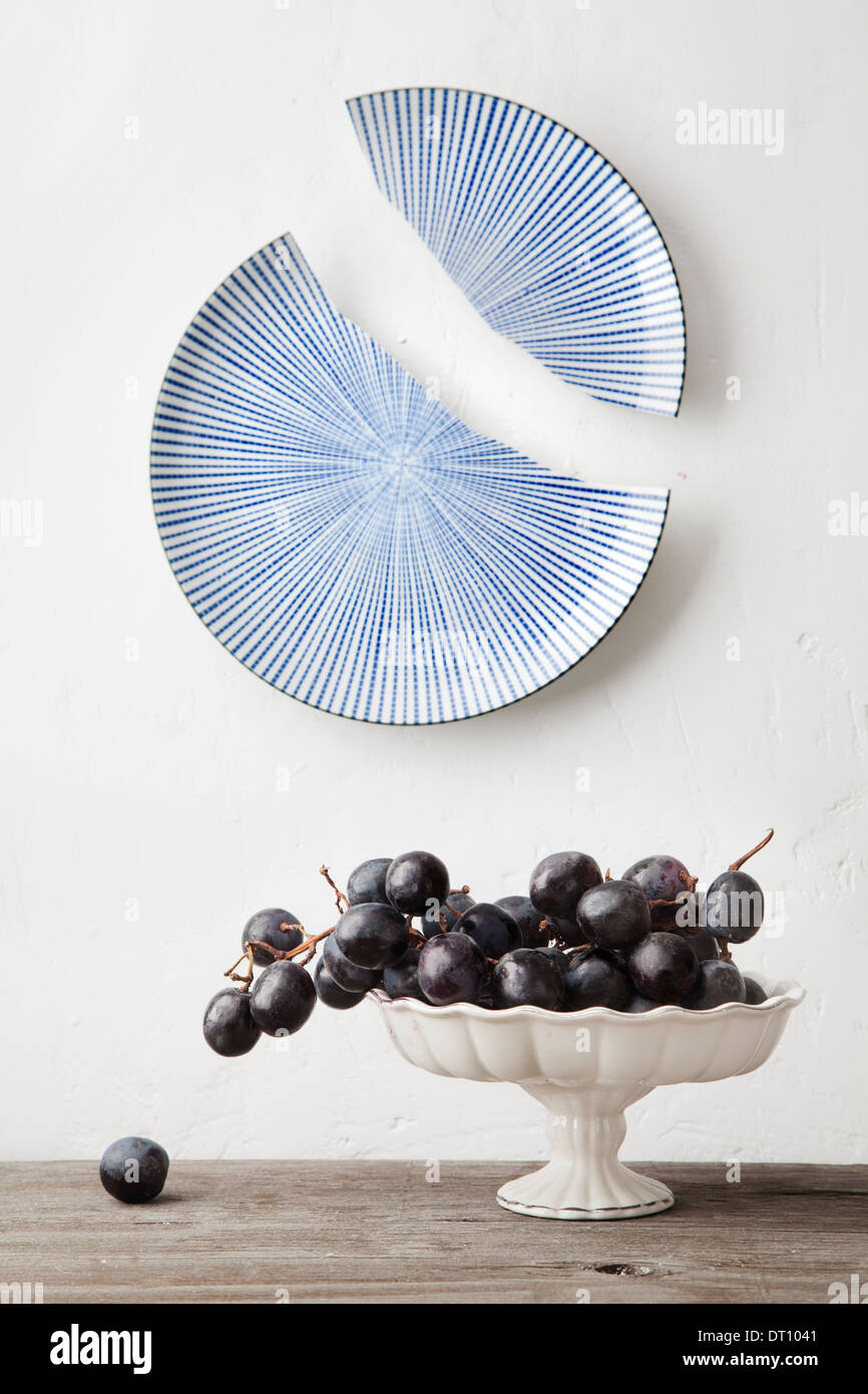 Bowl full of red grapes, broken plate hanging on wall Stock Photo - Alamy