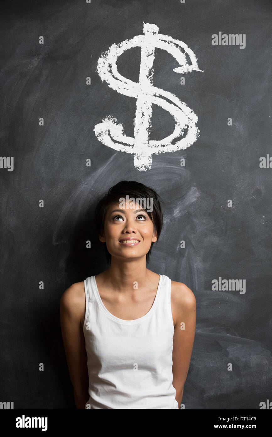 Happy Asian woman standing in front of dollar sign written on a ...