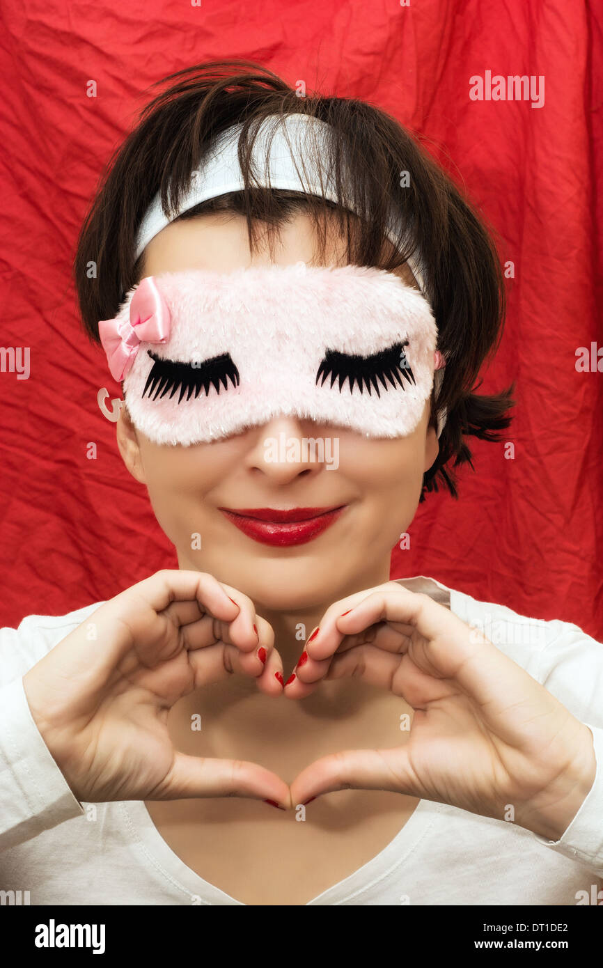 Attractive caucasian woman in sleeping mask making heart shape with her ...