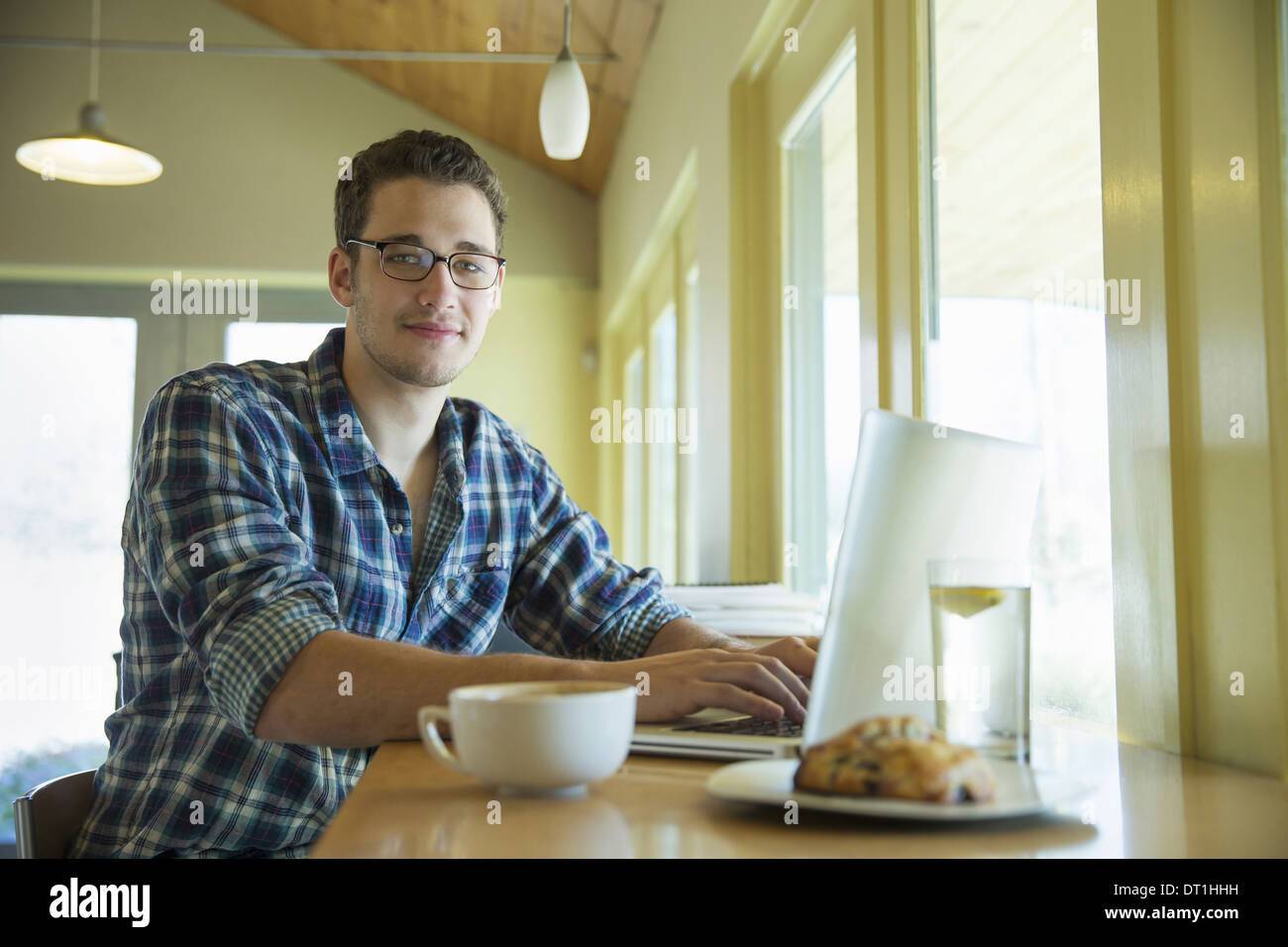 A young man sitting at a table using a laptop computer Stock Photo - Alamy