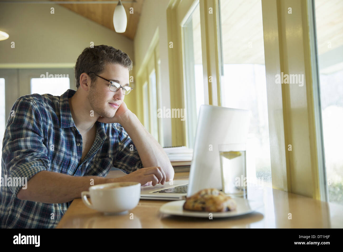 A young man sitting at a table using a laptop computer Stock Photo - Alamy