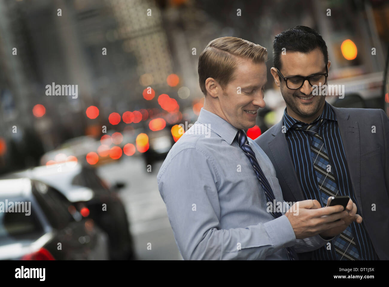 Two men standing together looking at a cell phone display on a busy ...