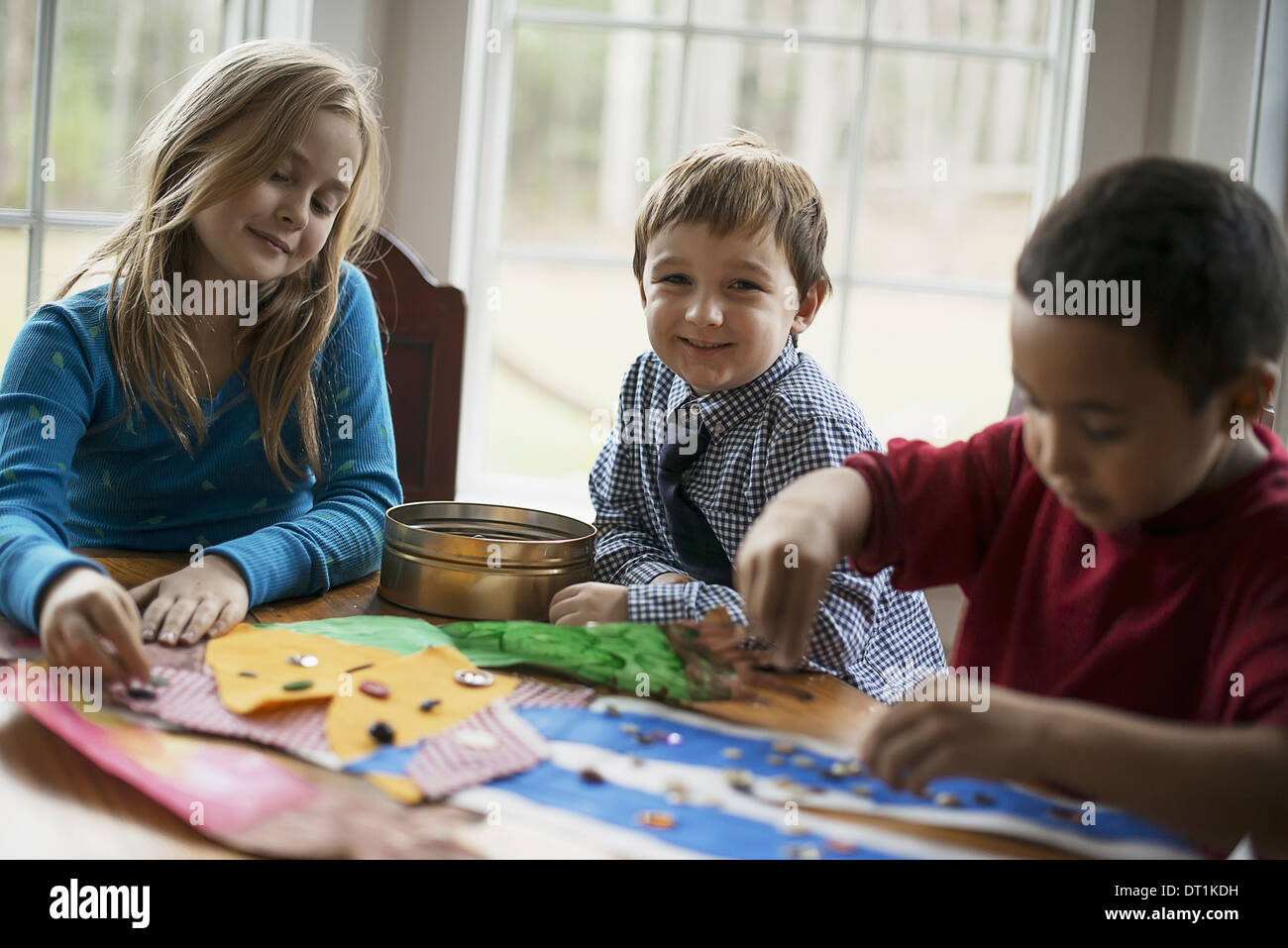 Children in a family home Three children creating pictures with glue ...