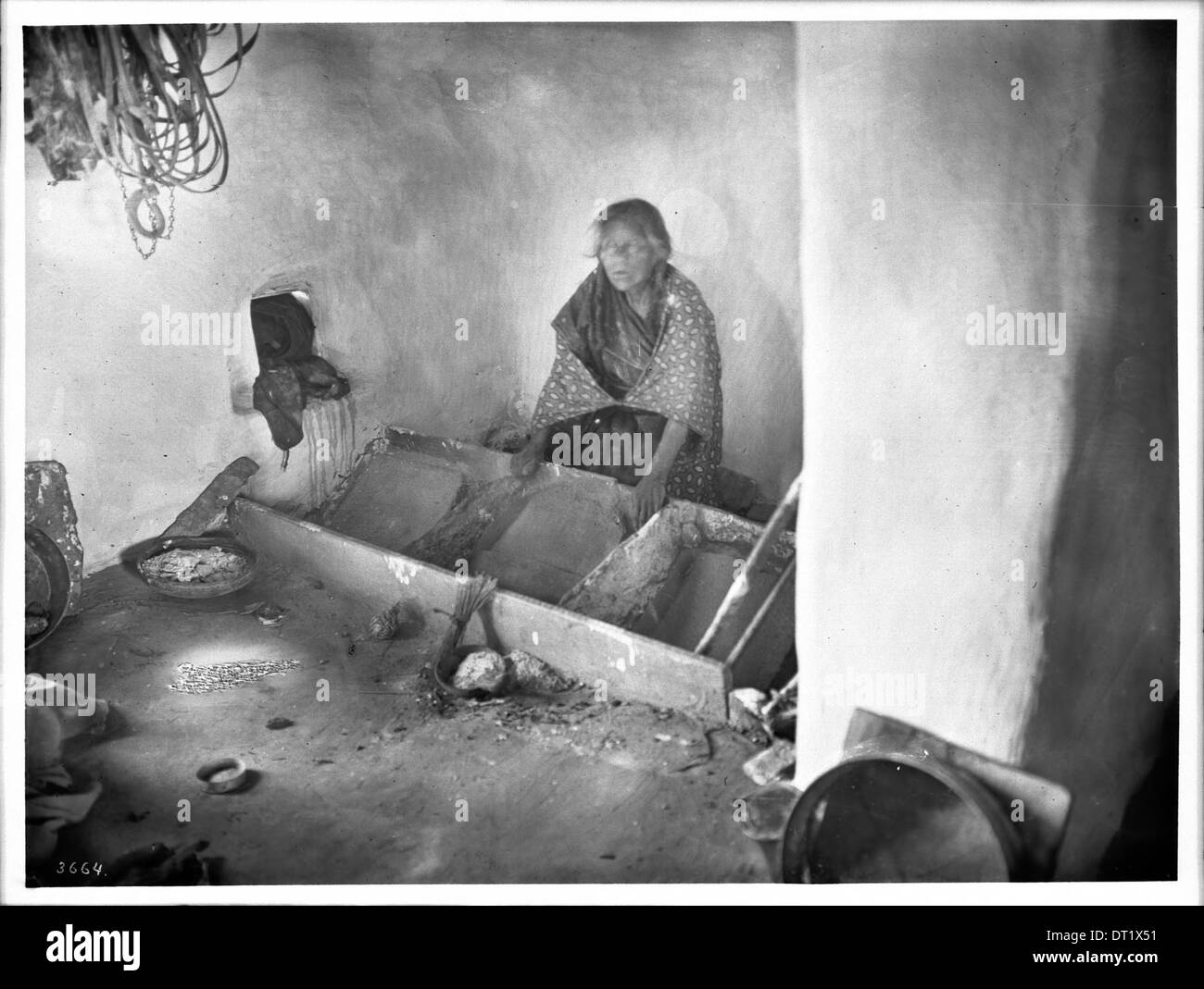 An elderly Hopi Indian woman is shown grinding corn to prepare bread ...