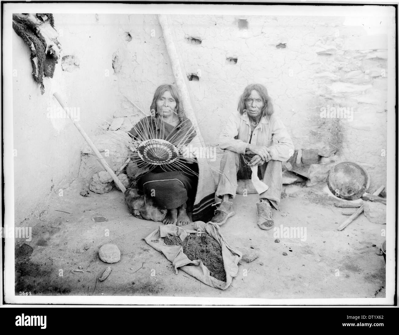 A Hopi woman is weaving a basket while her husband is photographed ...