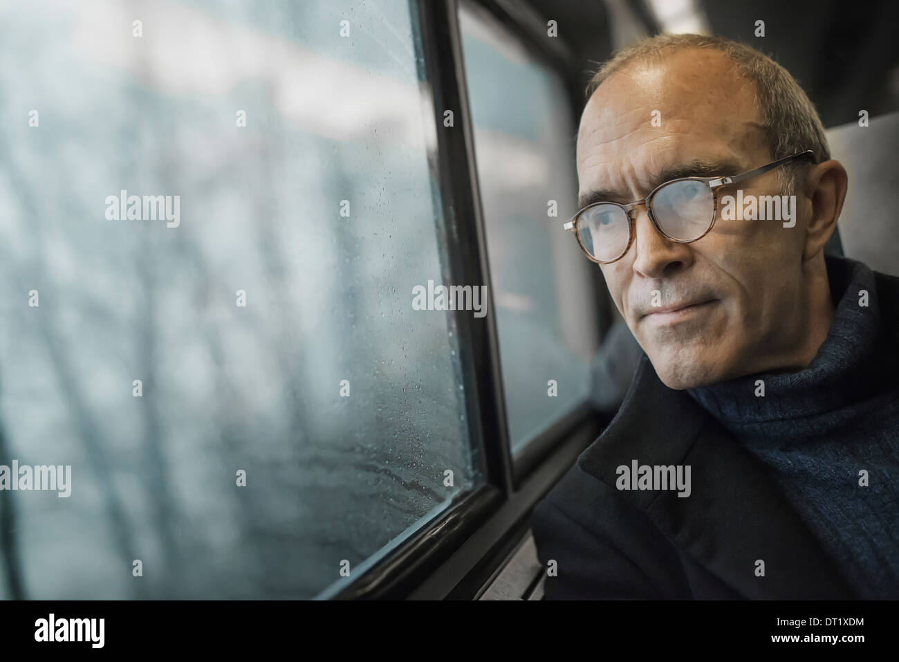 A mature man sitting in a window seat on a train journey looking out ...
