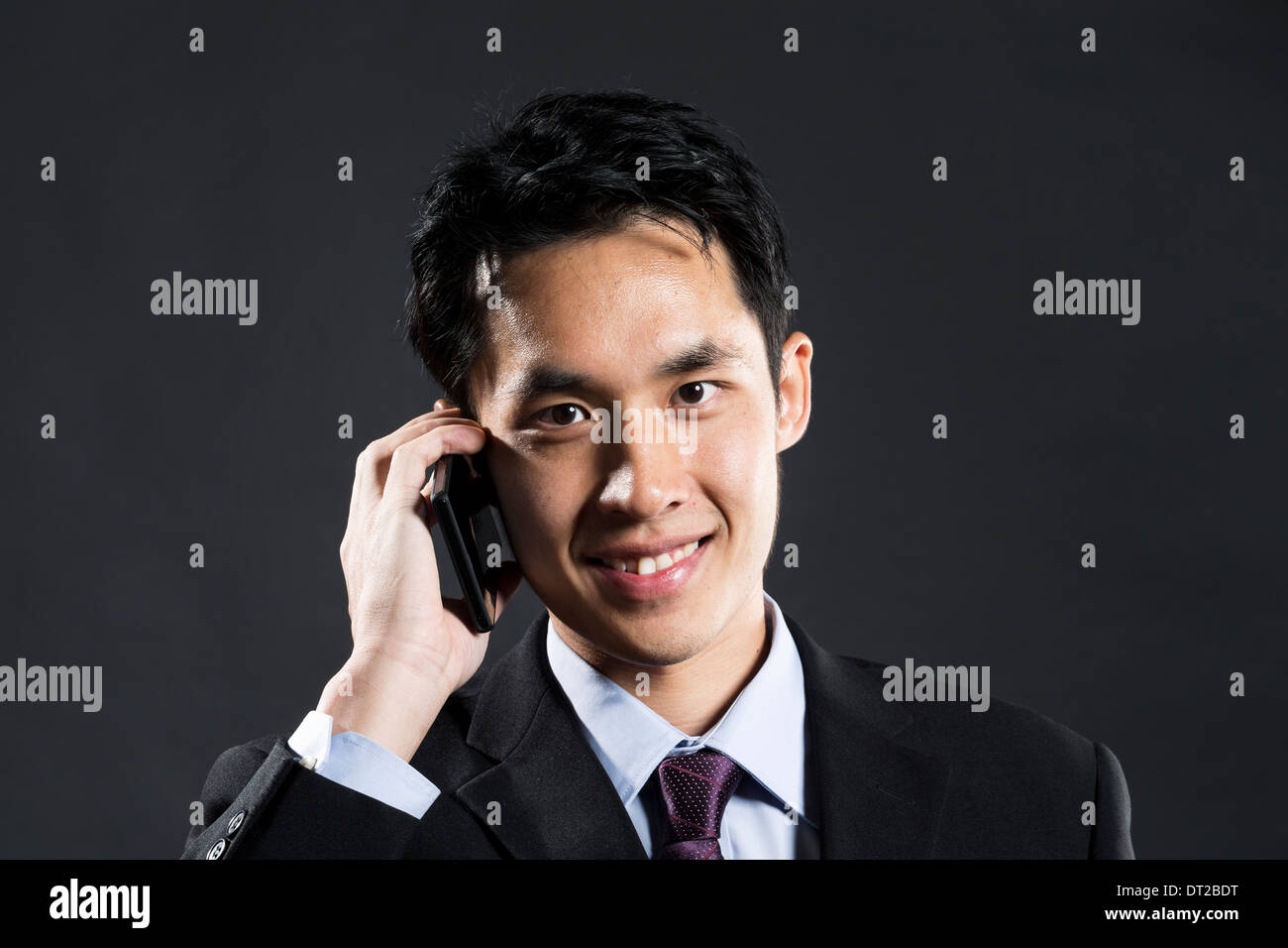 Portrait of a stylish Asian business man using a smart phone. Dark grey ...