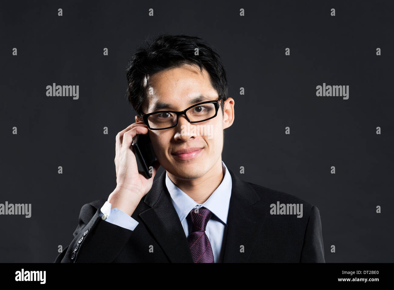 Portrait of a stylish Asian business man using a smart phone. Dark grey ...