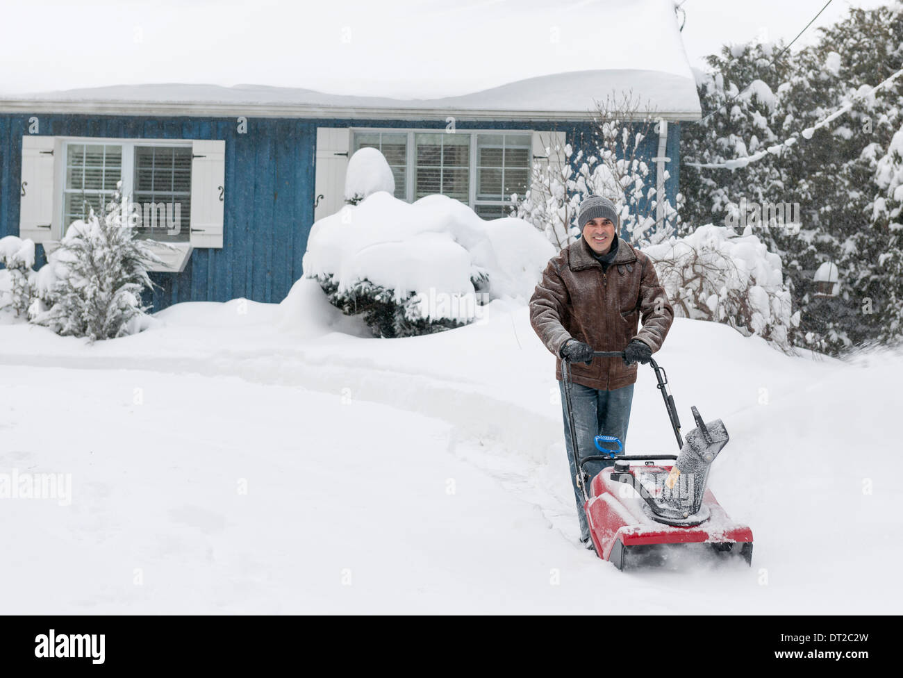 Man using snowblower to clear deep snow on driveway near residential ...