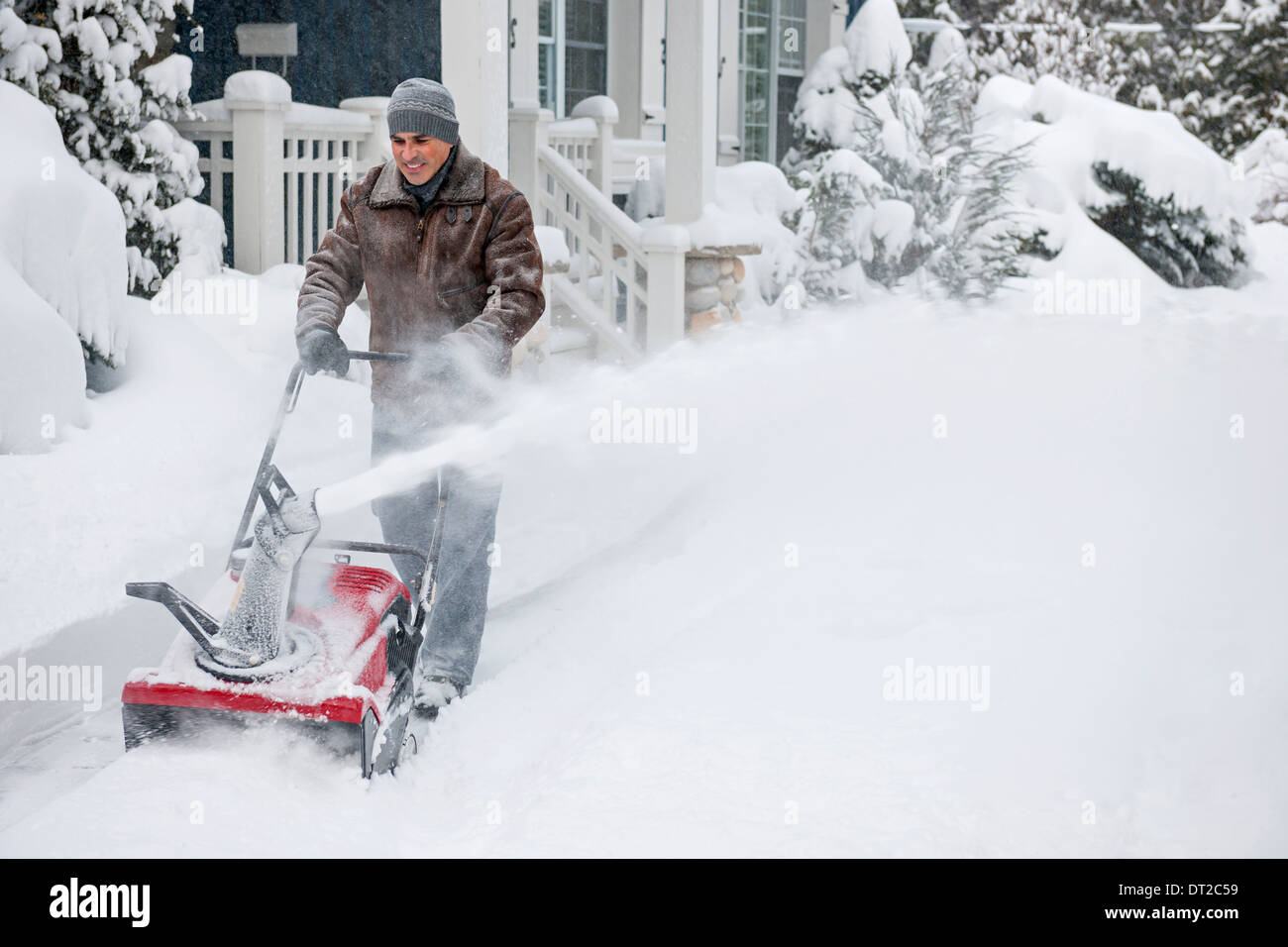 Man using snowblower to clear deep snow on driveway near residential ...