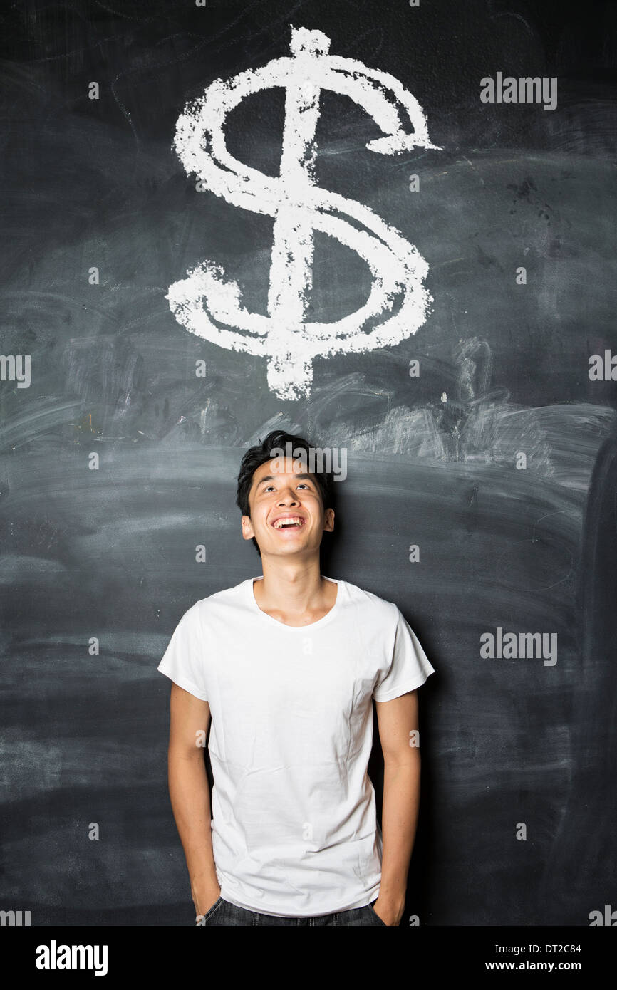 Happy Asian man standing in front of dollar sign written on a ...
