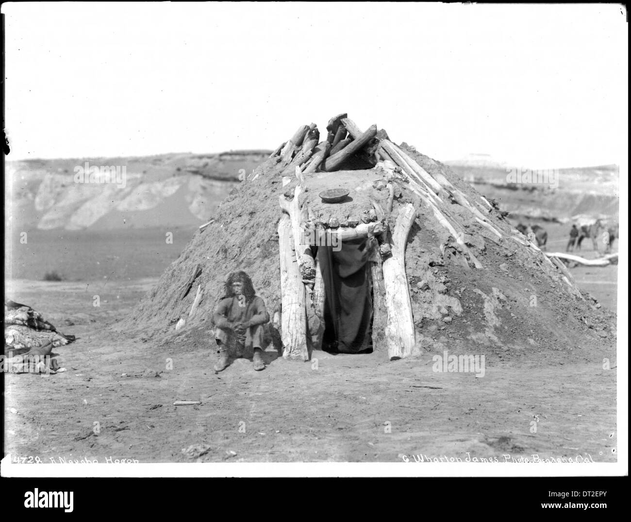 This photograph shows a Navajo man sitting in front of his hogan, taken ...