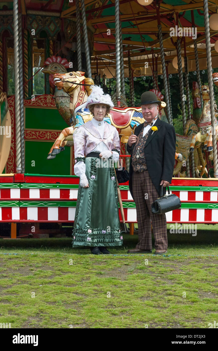 Man and woman dressed in Victorian period costume next to a carousel ...
