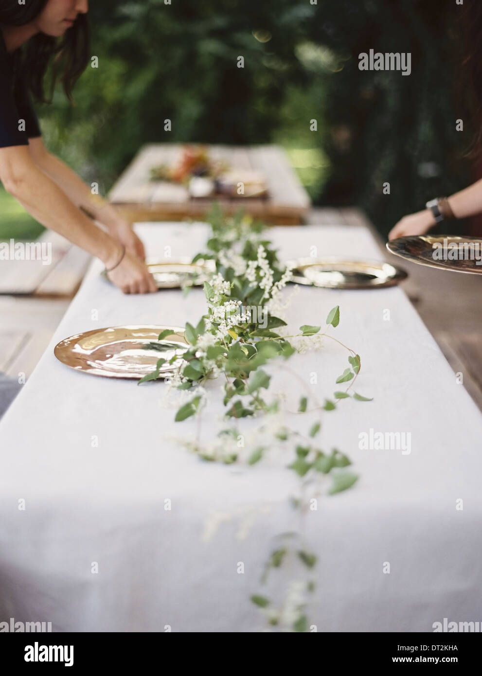 Two people leaning over a table laid outside with a white cloth and a ...