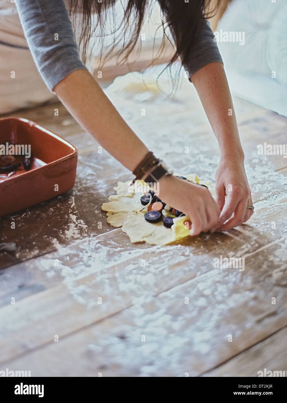 A domestic kitchen A woman creating an open pastry tart with vegetables ...
