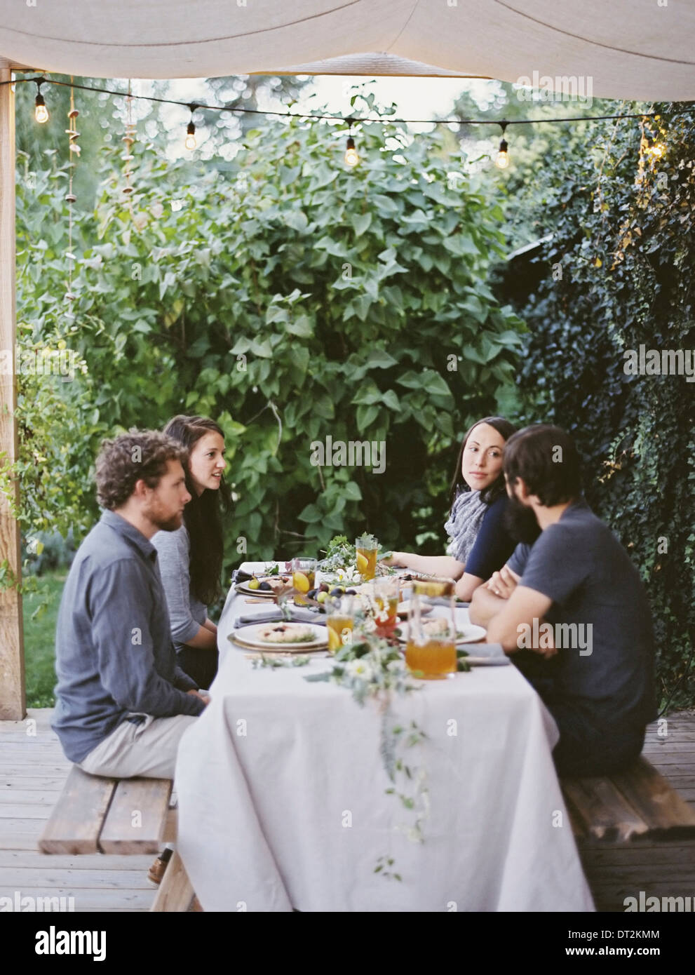Four people seated at a table in the garden Place settings and ...