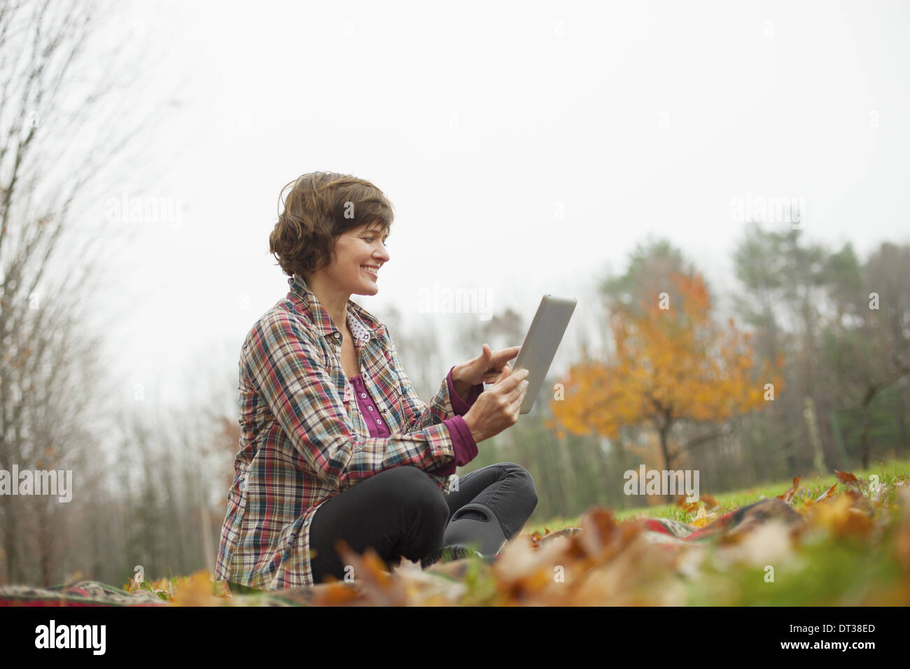A woman using a computer tablet sitting on the ground. Autumn leaves ...