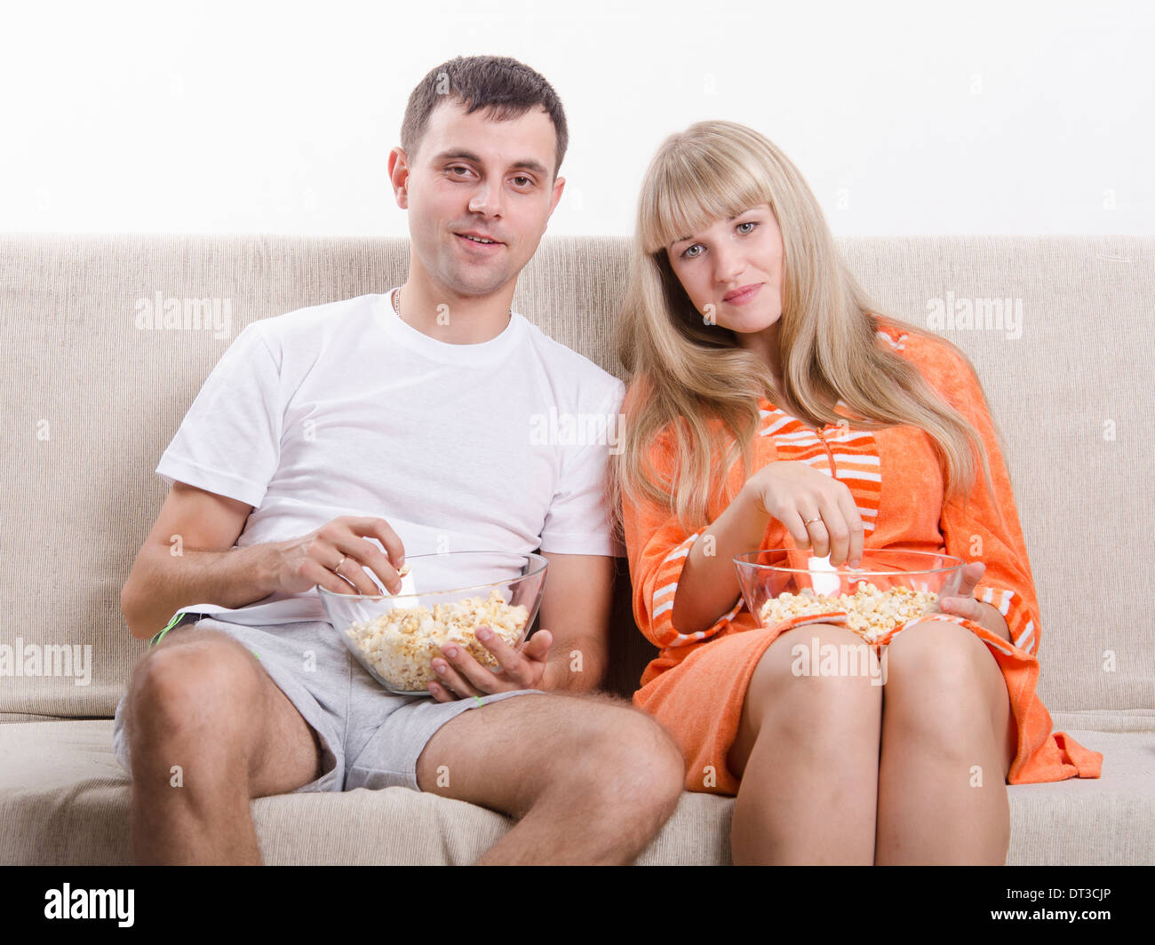 Couple sits on the couch. Each lap Cup of popcorn. Couple watching TV ...