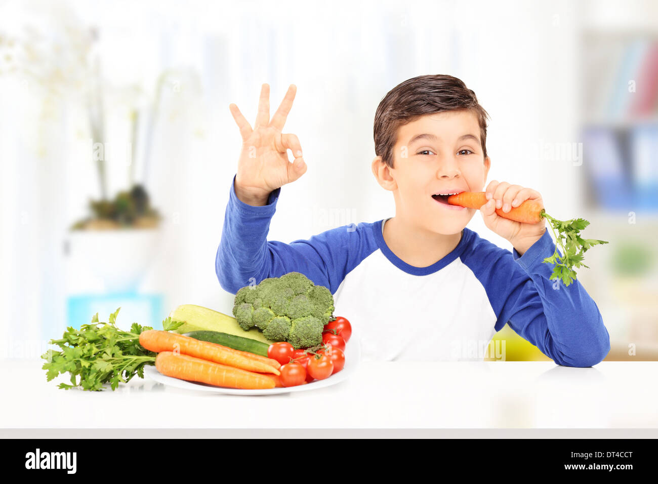 Boy eating vegetables and gesturing happiness with hand seated at table ...
