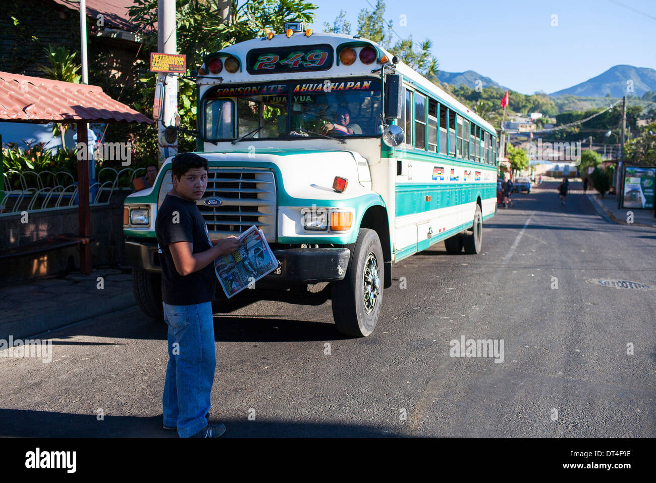 A bus conductor reads a newspaper in front of an old school bus being ...