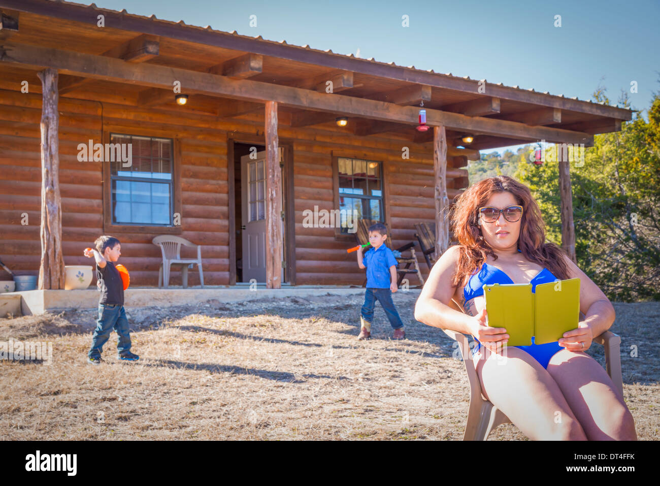 Mother on vacation reading on ebook reader while children playing in ...