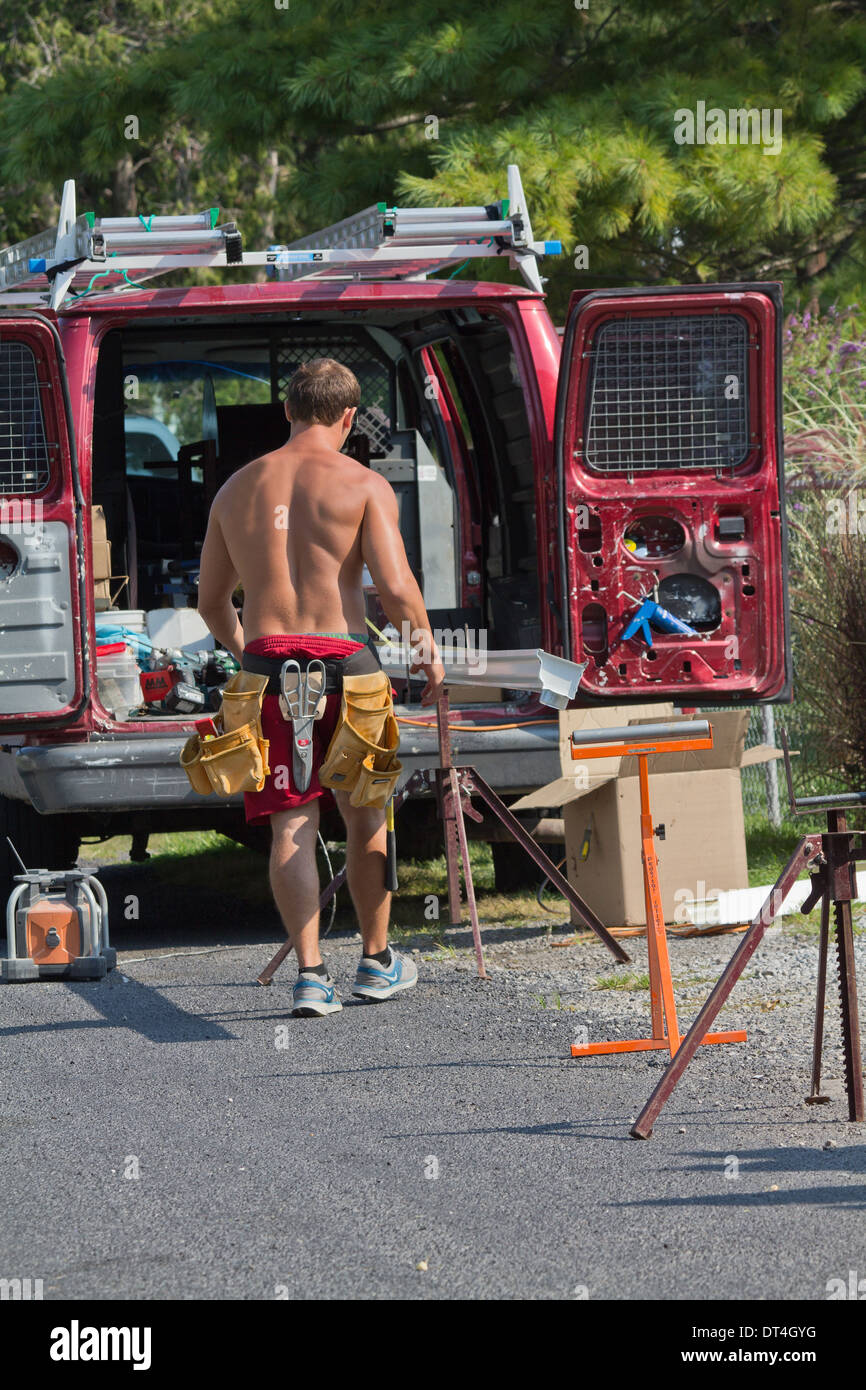 A construction worker instalating house roof rain gutter tool belt with ...